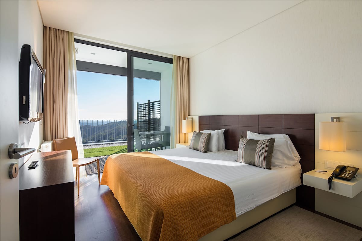Quarto de hotel com uma cama grande, uma escrivaninha, uma cadeira, um telefone e vista para o exterior.