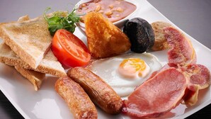 Um prato de comida de café da manhã com torradas, linguiça, bacon, ovos e feijão.
