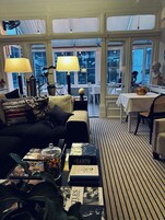 Uma sala de estar acolhedora com um sofá, uma mesa de centro com livros e vista através de amplas janelas.