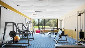 Uma academia com equipamentos de ginástica, grandes janelas e carpete estampado.