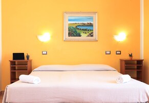 Quarto de hotel com cama, duas mesinhas de cabeceira, um quadro e arandelas de parede.