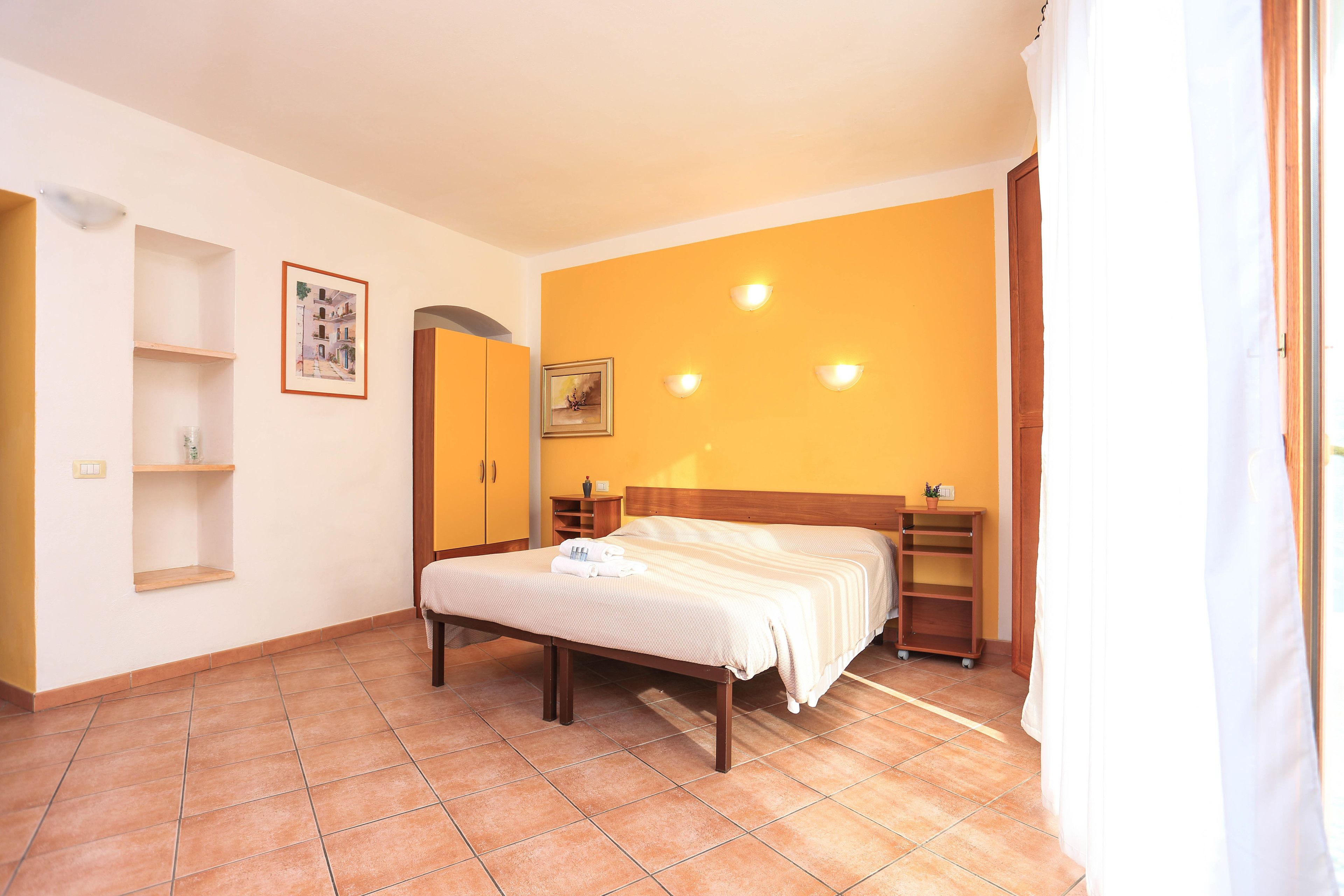 Um quarto com uma cama, mesa de cabeceira, guarda-roupa e prateleira com um quadro.