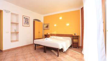Um quarto com uma cama, mesa de cabeceira, guarda-roupa e prateleira com um quadro.