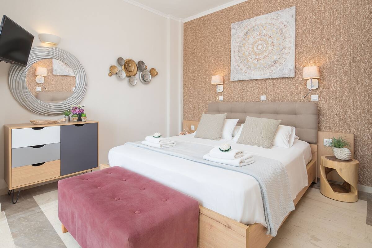 Quarto moderno com cama, mesas de cabeceira, televisão e espelho fixado na parede.
