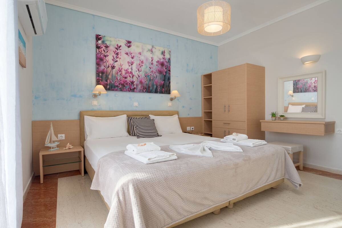 Quarto moderno com cama grande, mesas de cabeceira, guarda-roupa e prateleira na parede.