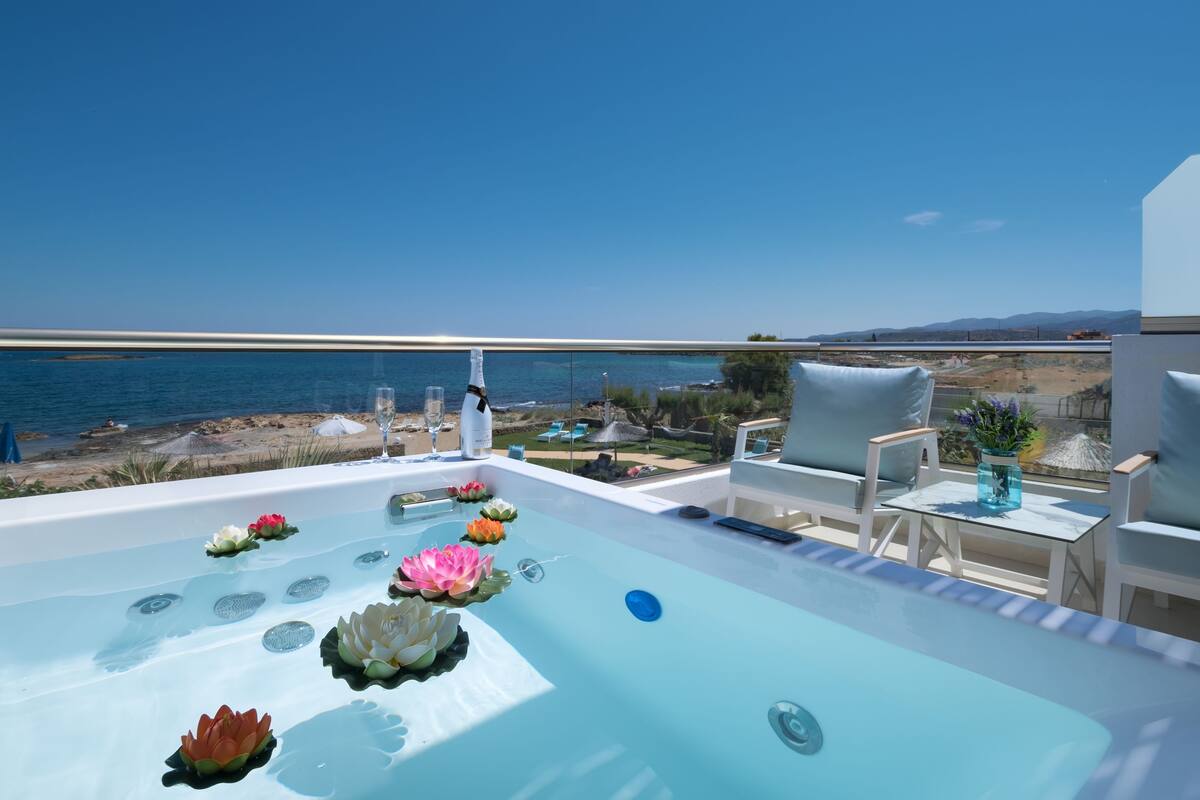 Banheira de hidromassagem com flores de lótus, um copo de vinho e vista para o mar.