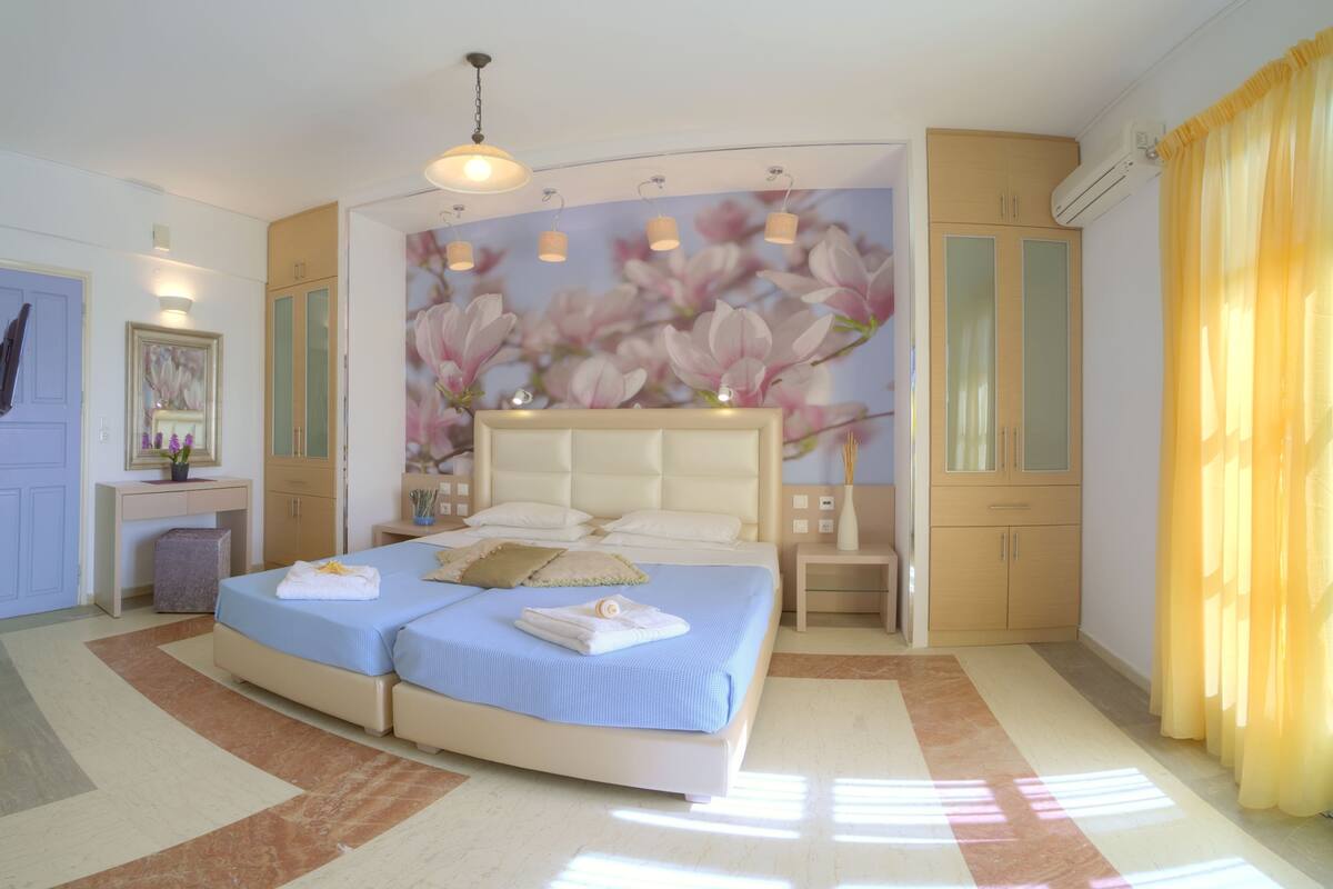 Quarto com cama de casal, mesa de cabeceira, cômoda e parede com um mural floral.