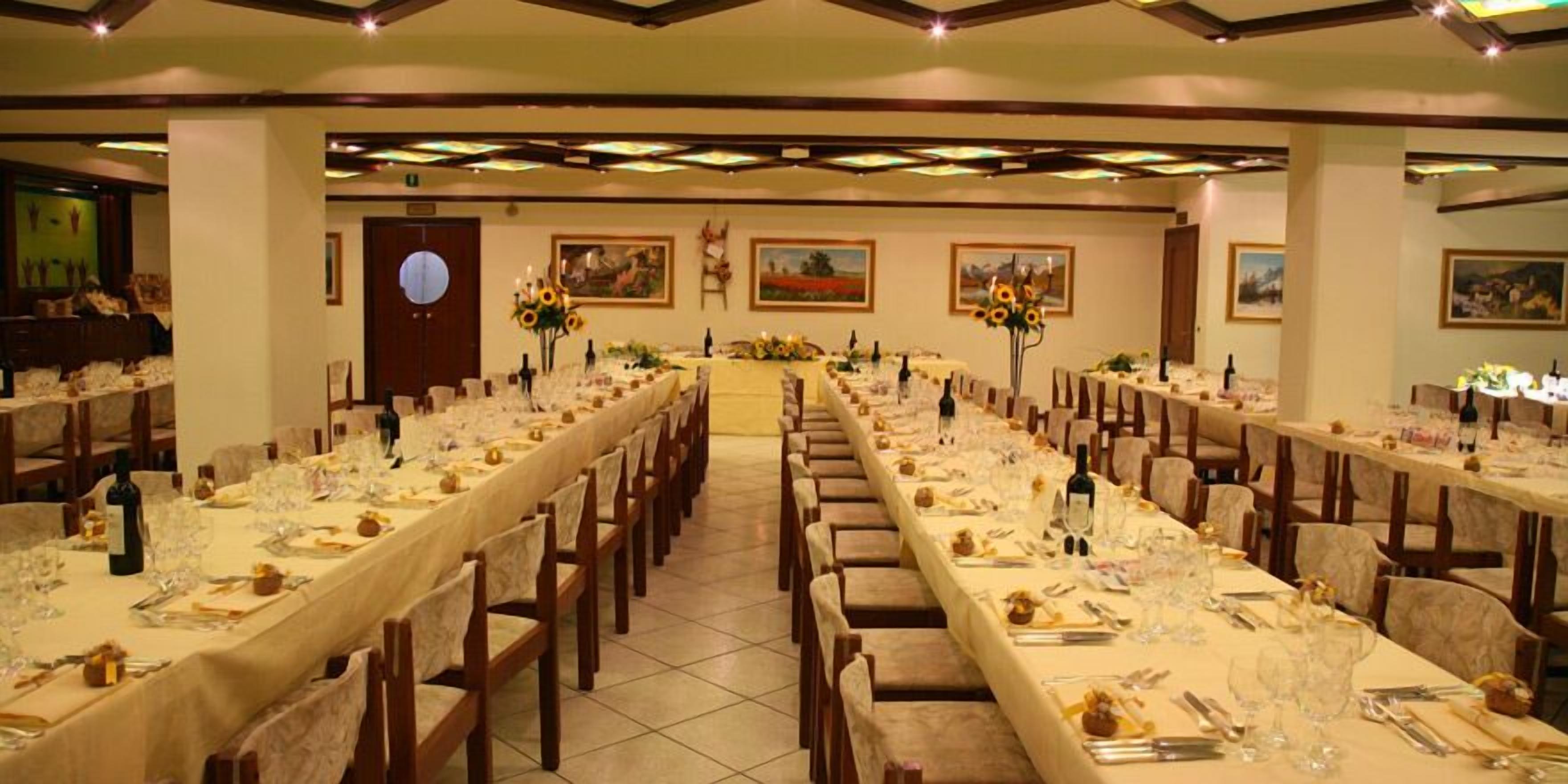 Salão de festas com longas mesas preparadas para refeições, obras de arte nas paredes e um candelabro.