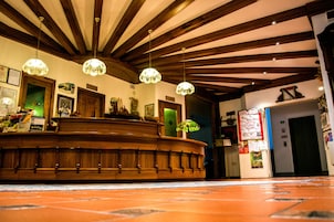 Uma área de recepção com balcão de madeira, luminárias pendentes e piso ladrilhado.