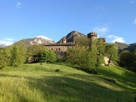 Um castelo com uma torre, rodeado por campos verdes e montanhas.