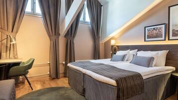 Quarto com cama grande, escrivaninha, cadeira e janela com cortinas.