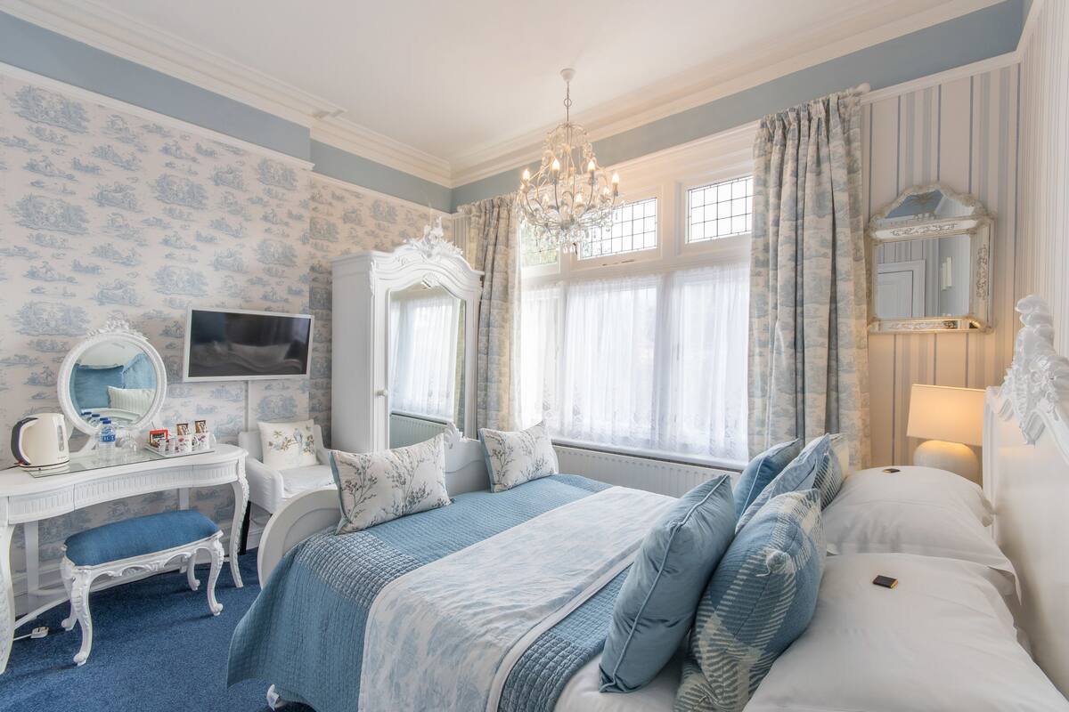 Quarto com cama, penteadeira com espelho, cômoda e janela com cortinas.