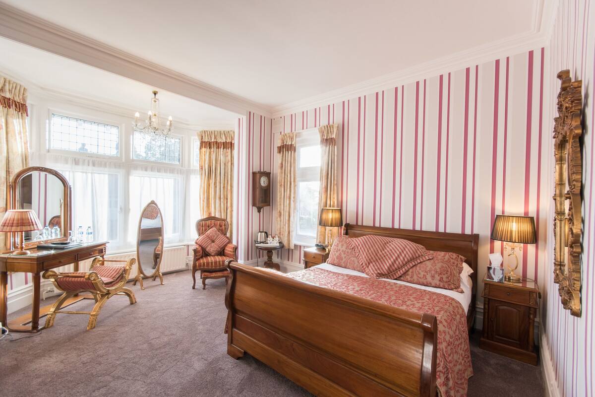 Um quarto clássico com cama de madeira, penteadeira, espelho e relógio.