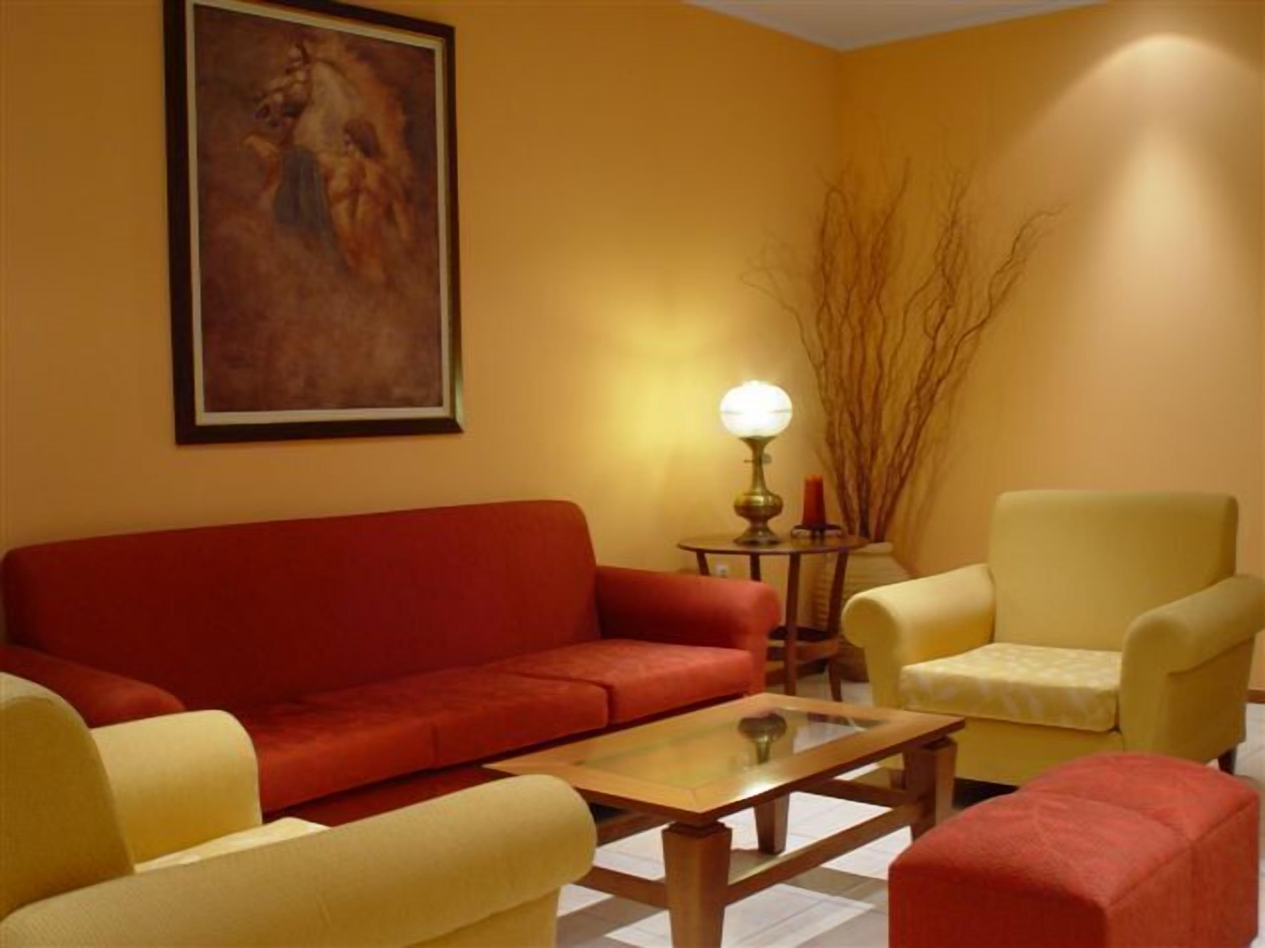 Uma sala de estar com um sofá vermelho, poltronas amarelas, uma mesa de centro de vidro e um quadro na parede.