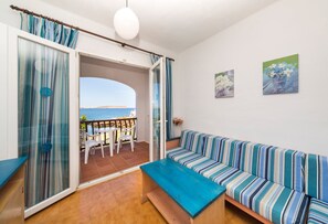 Uma varanda com vista para o mar, um sofá listrado e uma mesa com cadeiras.