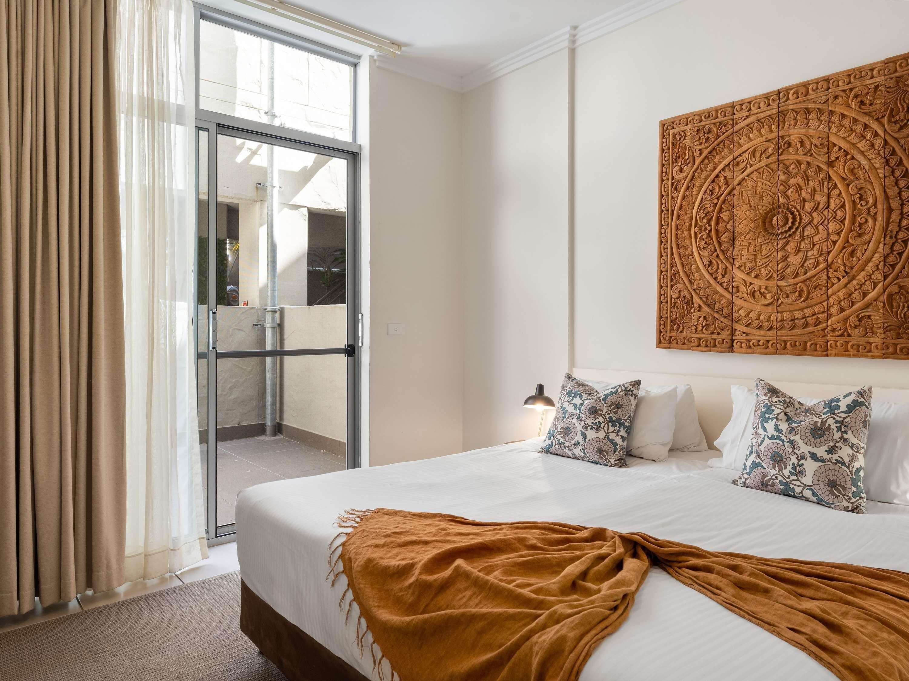 Quarto de hotel com cama, painel decorativo grande na parede e porta de vidro deslizante, com vista para o exterior.
