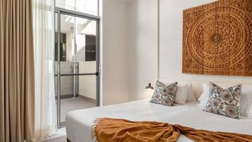 Quarto de hotel com cama, painel decorativo grande na parede e porta de vidro deslizante, com vista para o exterior.