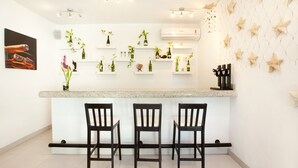 Uma cozinha moderna com bancada de mármore, três cadeiras de madeira e prateleiras com plantas e utensílios de cozinha.