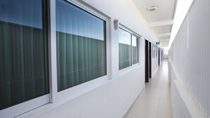 Um corredor comprido e estreito, com grandes janelas de um lado e uma parede branca do outro.