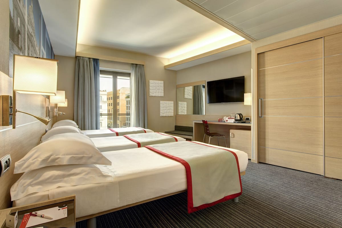 Quarto de hotel com duas camas, uma escrivaninha, uma cadeira, televisão e armário.