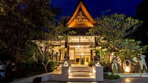 Entrada do resort com uma placa de destaque, degraus que levam à entrada e vegetação ao redor.