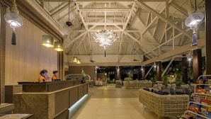 Um hall amplo com teto alto, balcão de recepção, móveis de vime e um candelabro.