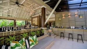 Uma área de bar moderna, com teto alto, vigas de madeira e balcão com banquetas.