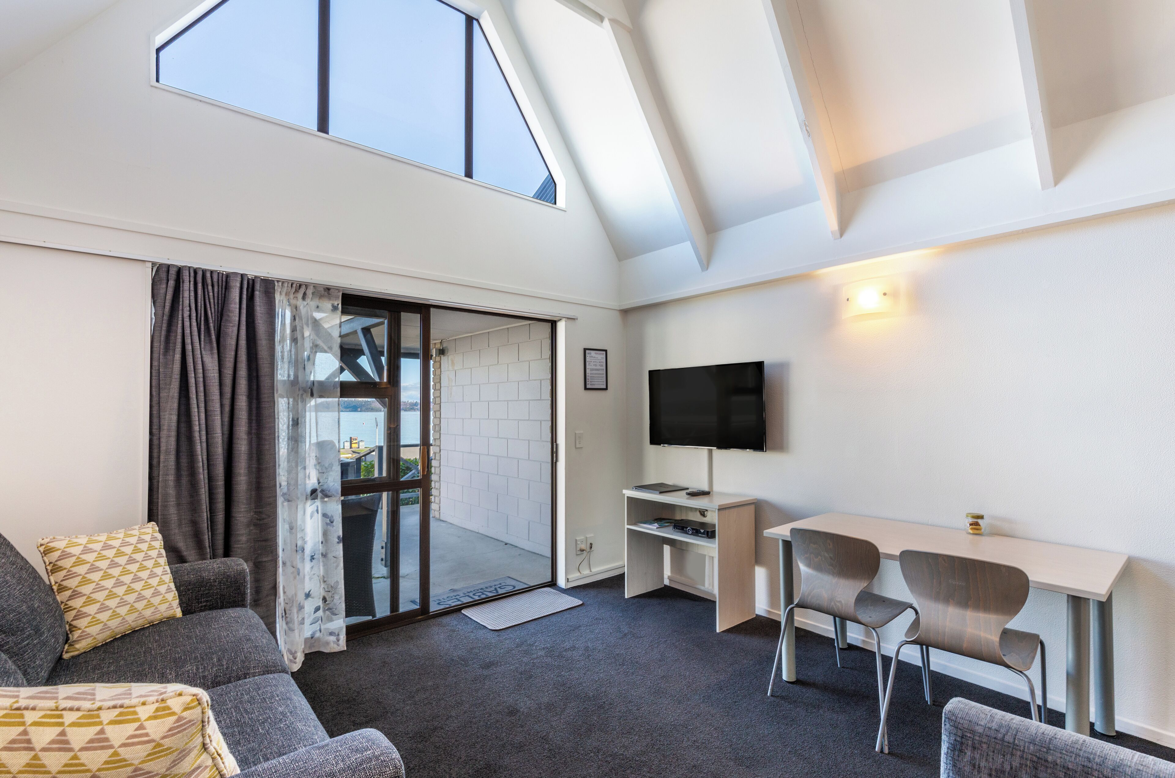 Quarto moderno com sofá, duas cadeiras, TV e porta de vidro deslizante para área externa.