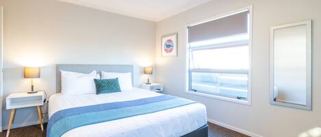 Quarto de hotel com cama, mesas de cabeceira, janela e espelho fixado na parede.