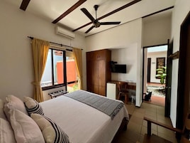 Quarto com cama, escrivaninha, televisão e ventoinha no teto.