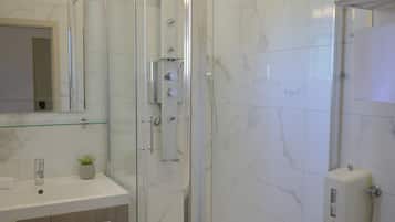 Um banheiro moderno com chuveiro em box de vidro, pia branca com bancada de mármore e vaso sanitário.
