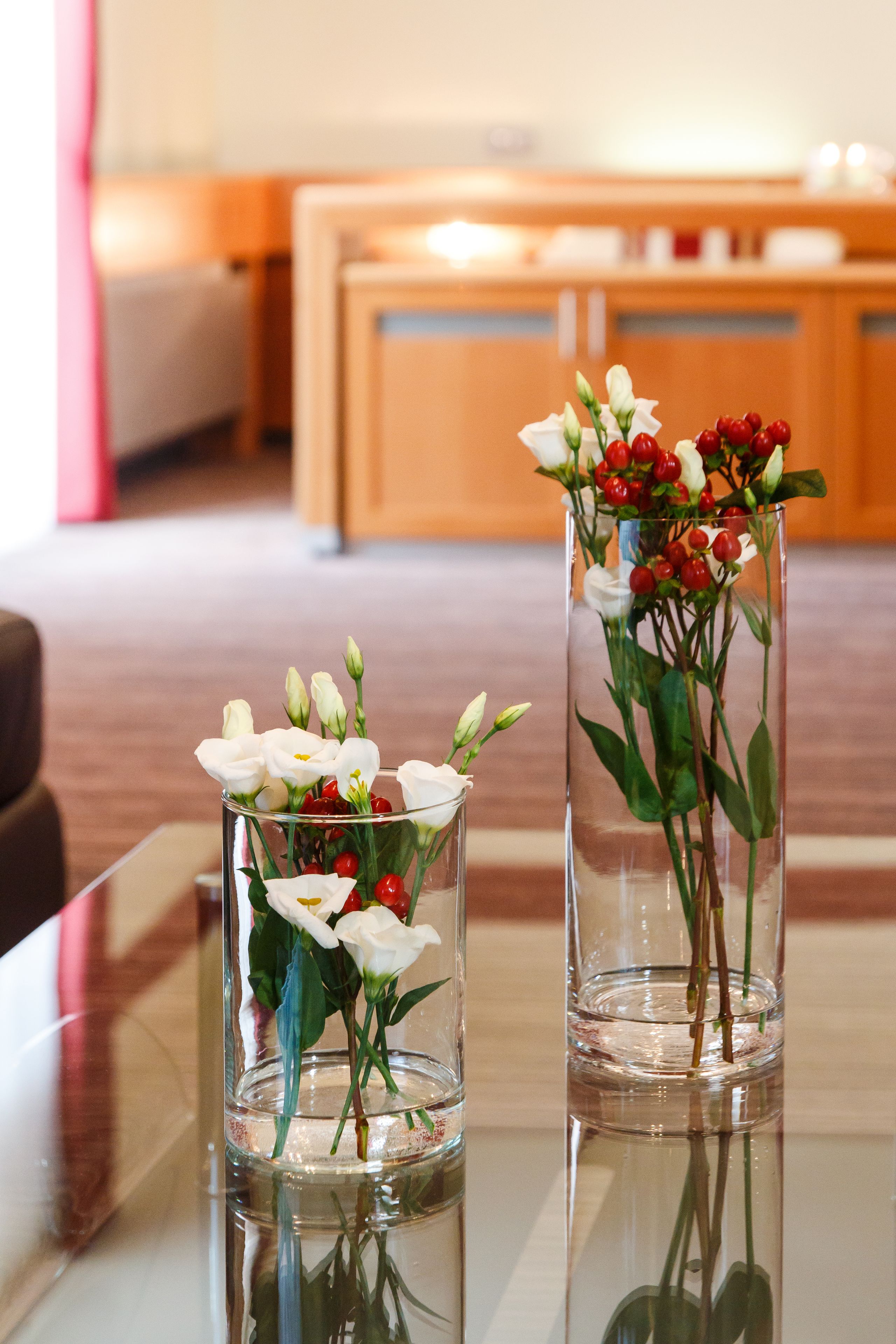 Dois vasos de vidro transparente com flores sobre uma superfície espelhada.