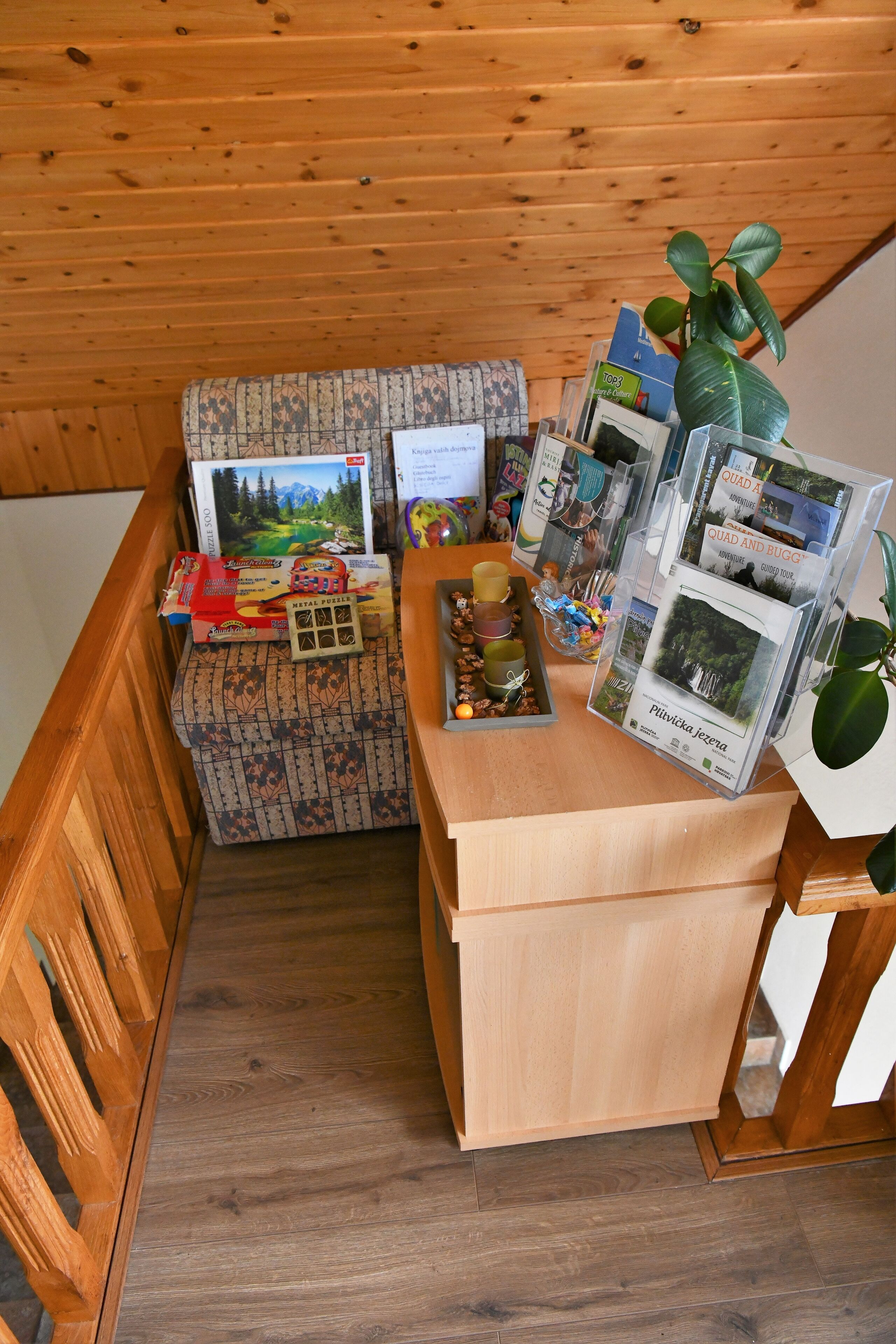 Interior de uma cabana de madeira, com uma escrivaninha de madeira, um banco estampado e vários objetos, incluindo uma planta, um porta-retrato e uma mesinha com bebidas.