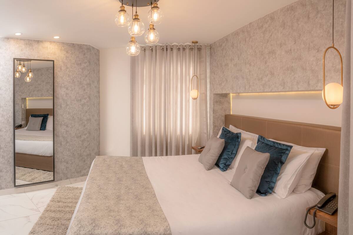 Um quarto moderno com uma cama grande, uma mesa de cabeceira com um telefone, um espelho e um lustre.