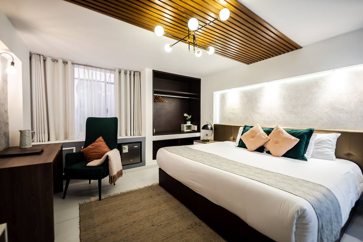 Quarto de hotel moderno com cama grande, escrivaninha, cadeira e guarda-roupa embutido.
