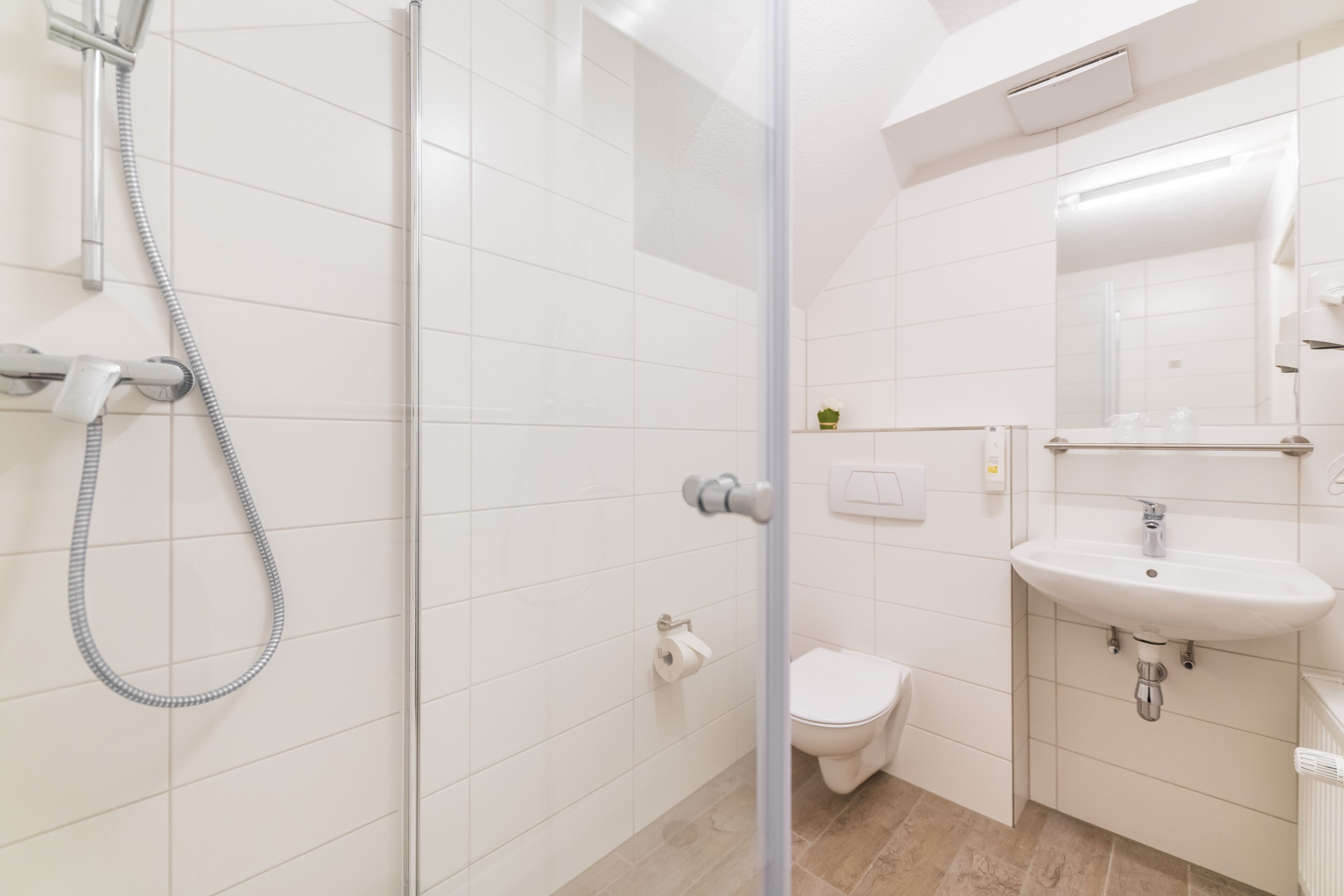 Um banheiro moderno com box de vidro, vaso sanitário e pia com espelho acima.