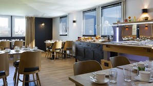 Uma sala de jantar com mesas postas para o café da manhã, cadeiras de madeira e um balcão com alimentos.
