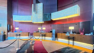 Uma área de recepção de hotel com design moderno, incluindo um balcão de atendimento, duas recepcionistas e um balcão de check-in.