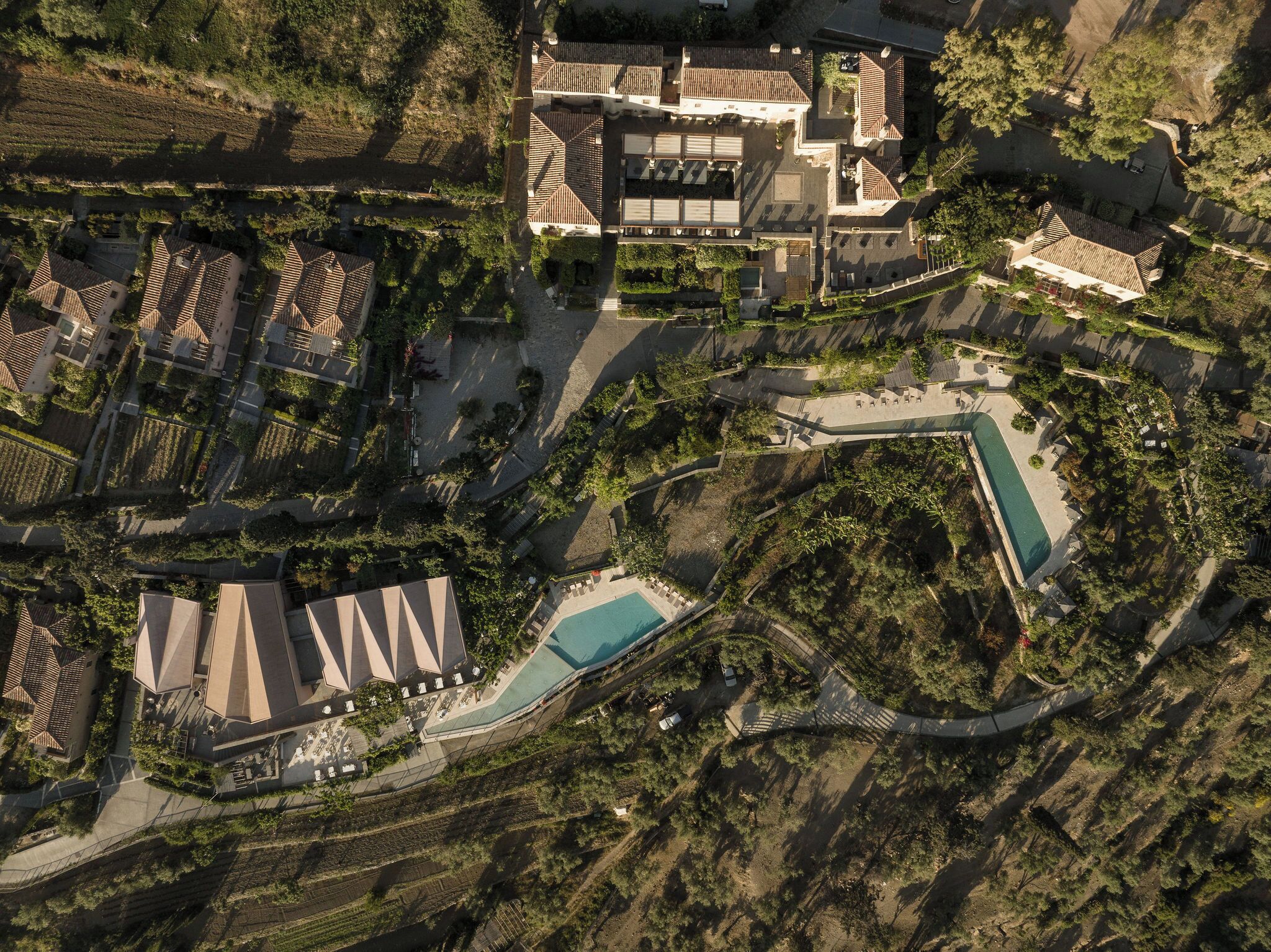 Vista aérea de um resort com vários edifícios, uma piscina grande e vegetação ao redor.