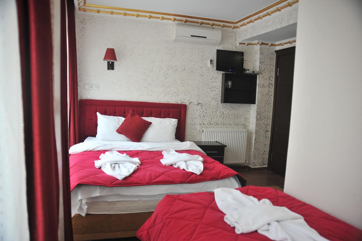 Quarto de hotel com colcha vermelha, almofadas brancas e cabeceira vermelha.