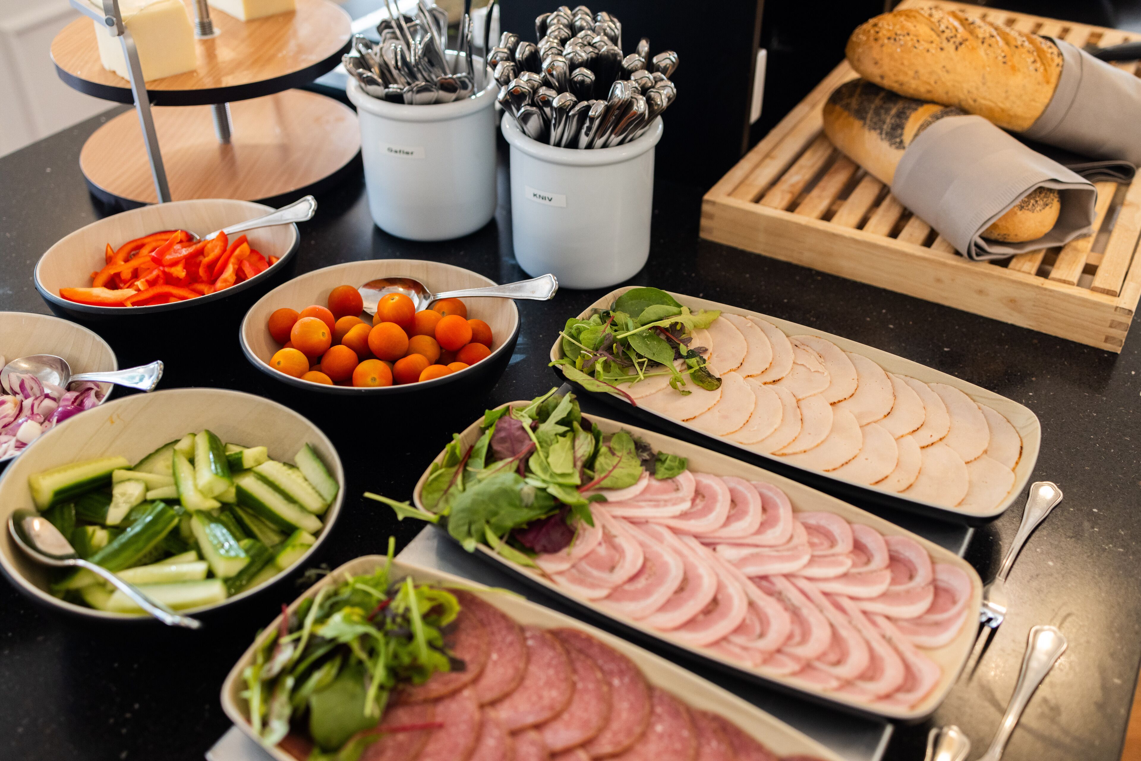 Mesa de buffet com diversos alimentos, incluindo carnes fatiadas, legumes e pão.