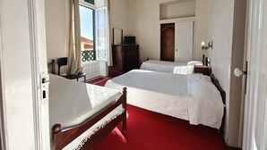Quarto com duas camas, cômoda, cadeira, janela com cortinas e porta.
