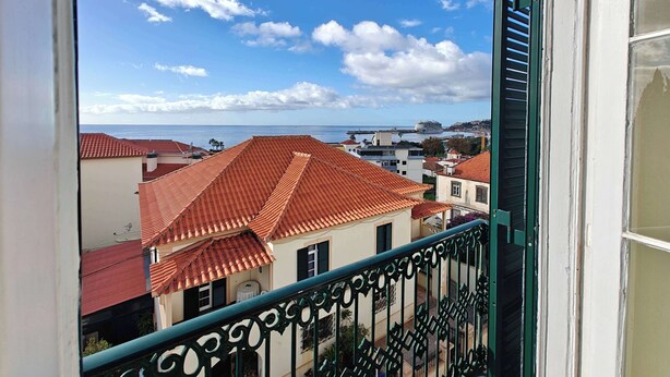 Uma varanda com vista para edifícios com telhados de terracota e o mar.