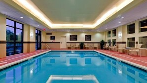 Piscina interna com água cristalina, rodeada por espreguiçadeiras e piso de ladrilho vermelho.