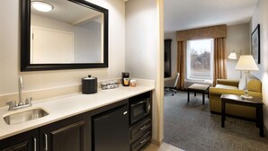 Quarto de hotel com cozinha compacta, um espelho grande, sofá e janela com cortinas.