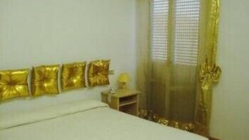 Um quarto com uma cama, uma mesinha com abajur e uma janela com cortina.