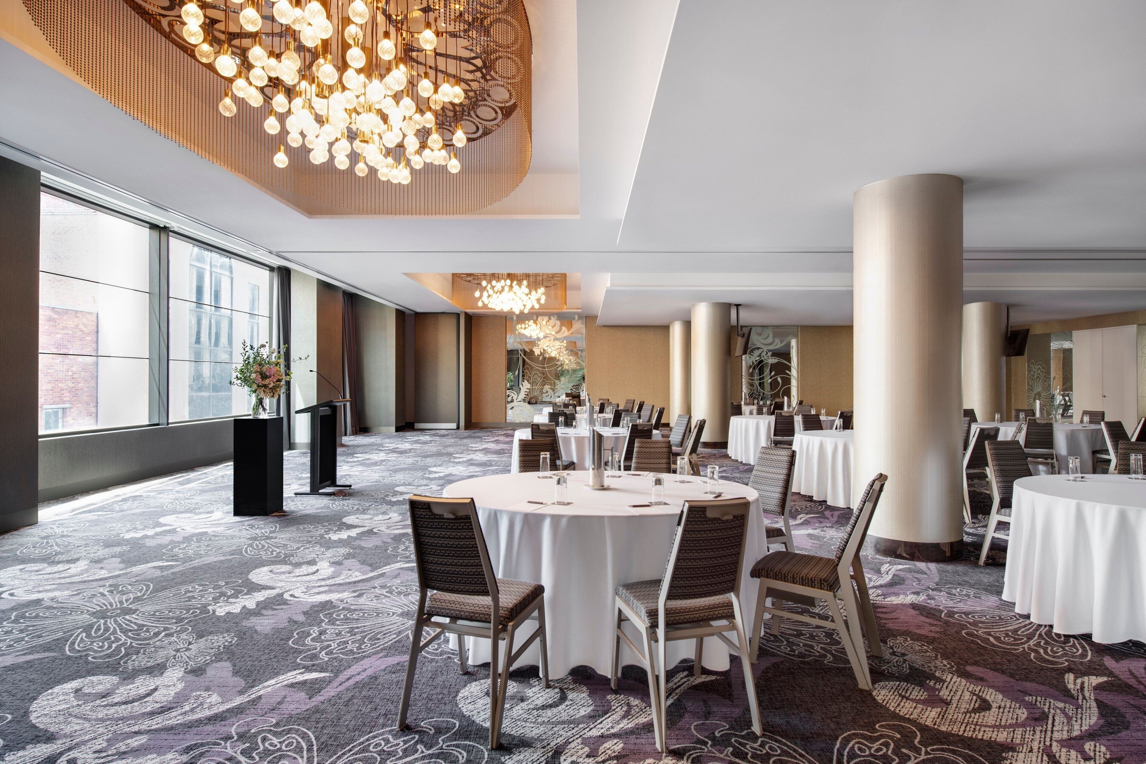 Um amplo salão de banquetes com mesas redondas, cadeiras e um lustre decorativo.