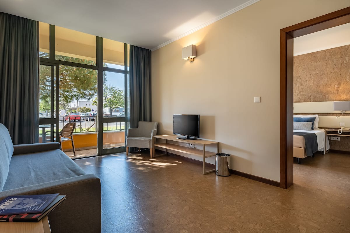 Quarto de hotel moderno com sofá, TV e vista para o exterior.