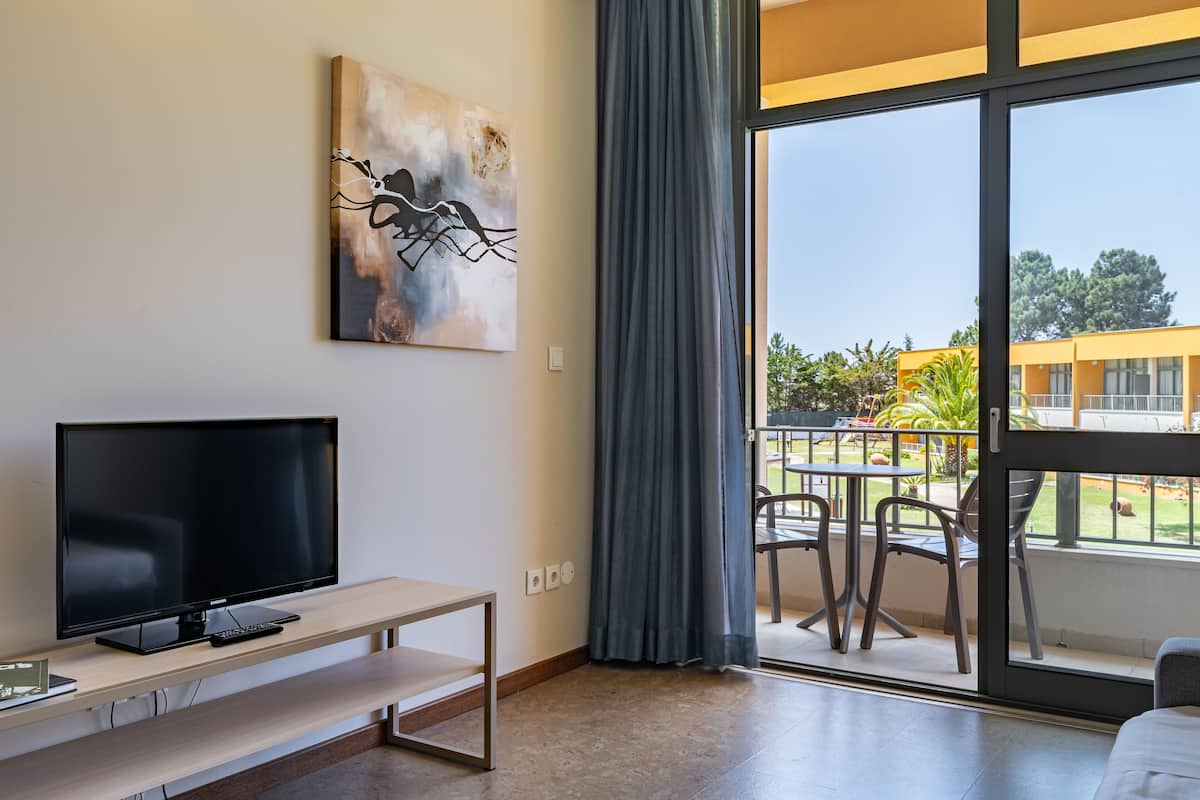 Quarto de hotel moderno com televisão de tela plana em console de madeira, um quadro na parede e uma varanda com área de estar externa.
