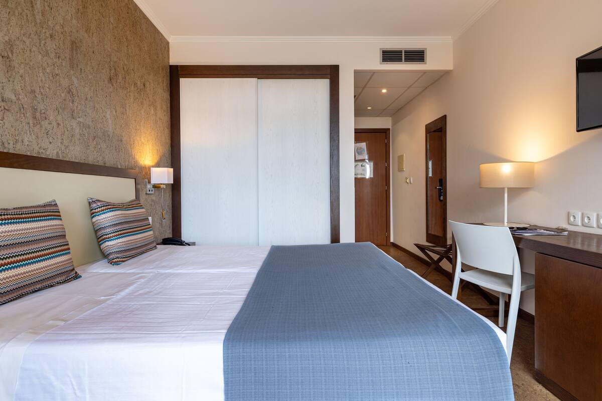 Quarto de hotel com cama, escrivaninha, cadeira e guarda-roupa.